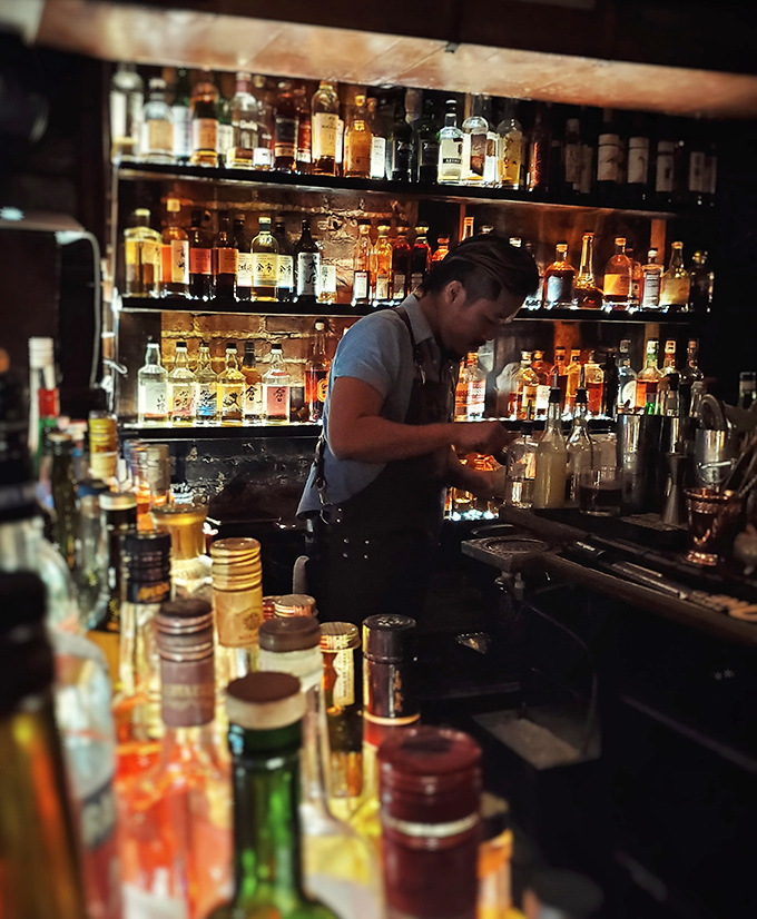 Staff: Mixologist at work, surrounded by an arsenal of spirits &ndash; part scientist, part artist, all dedicated to the perfect pour.