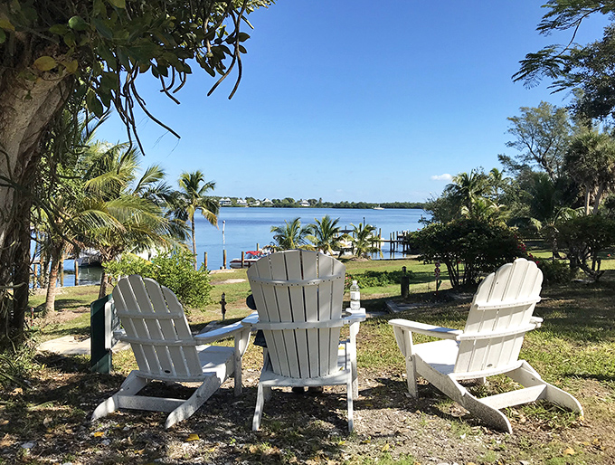 Three white Adirondack chairs face the water, silently inviting visitors to sit, breathe, and remember what vacation is actually supposed to feel like.