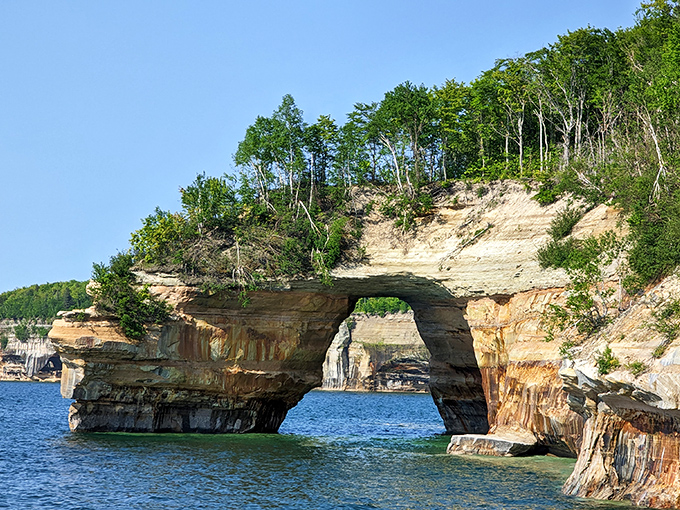 This magnificent stone arch seems almost deliberately crafted, a doorway between worlds where forest meets water in perfect harmony.