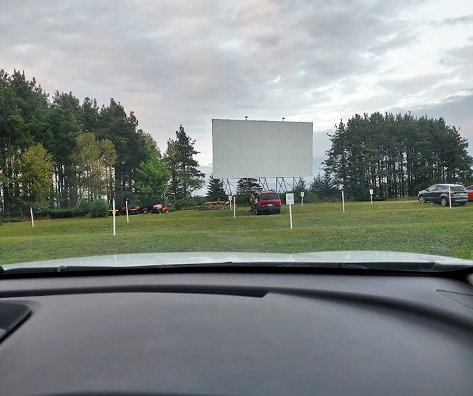 The dashboard perspective every drive-in veteran knows &ndash; framing the distant screen through windshield glass, anticipation building.