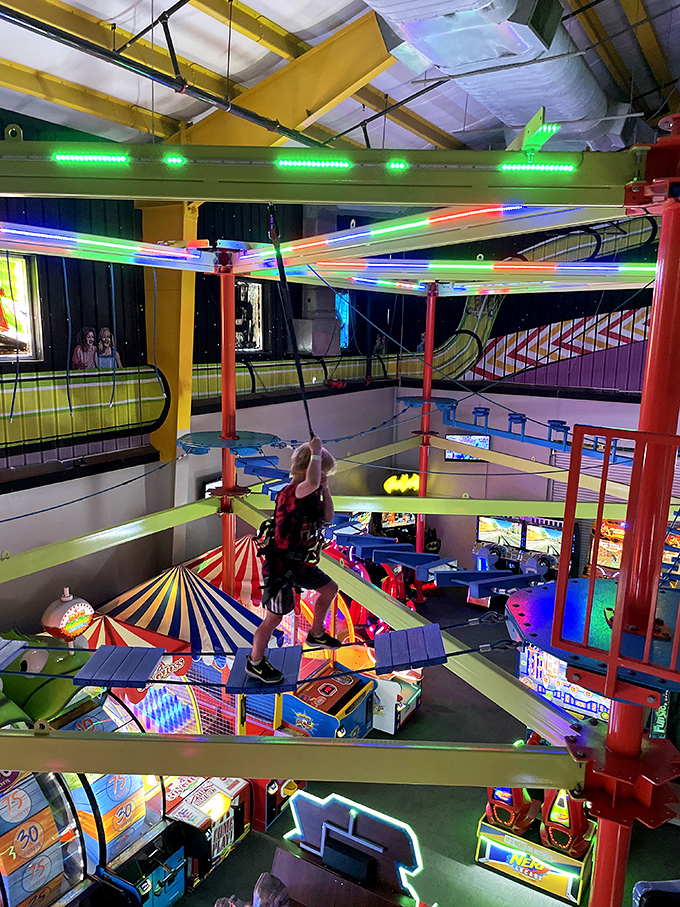 An indoor ropes course challenges visitors with a neon-lit aerial adventure suspended above the bustling arcade below.