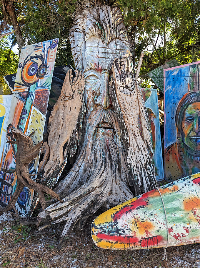 This ancient-looking face emerges from the wood as if awakening after centuries, hands raised in greeting or perhaps blessing.