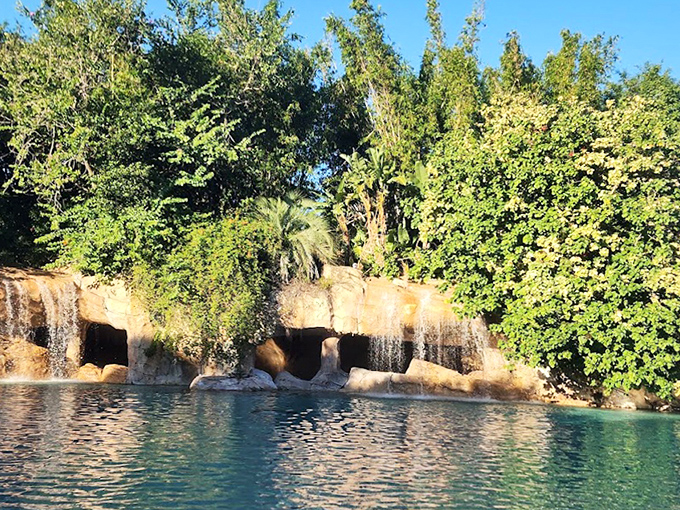 Gentle waterfalls spill over rock formations into crystal-clear waters, creating nature's perfect swimming hole surrounded by lush vegetation.