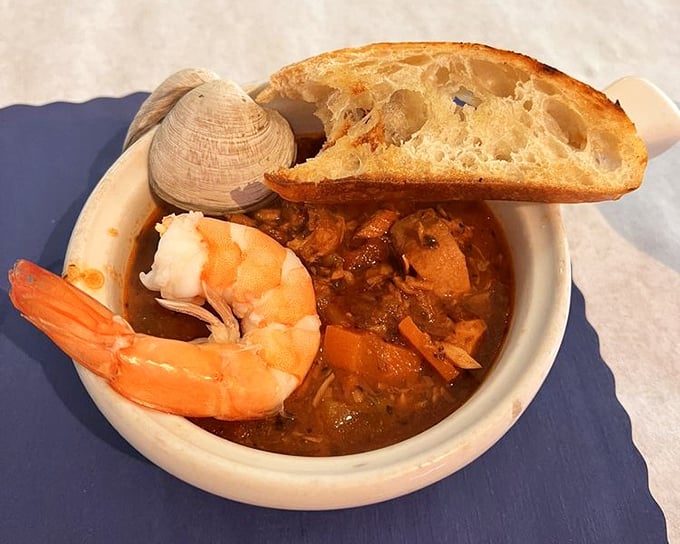 A tomato-rich broth cradles the day's freshest catch – where bread serves as both utensil and sponge for capturing every flavorful drop.