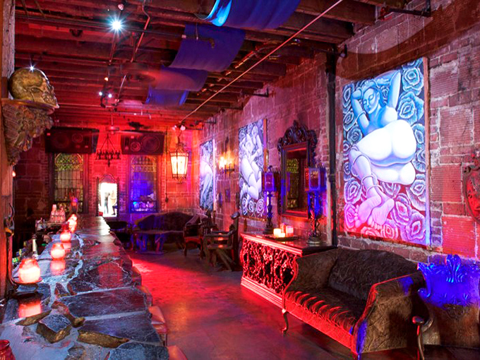 Dramatic lighting transforms brick walls into canvas-like backdrops for plush seating areas, creating intimate spaces for connection amidst the Gothic grandeur.