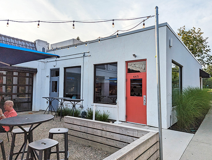 A simple white exterior with a welcoming red door proves that sometimes the most unassuming facades hide the most extraordinary culinary treasures.
