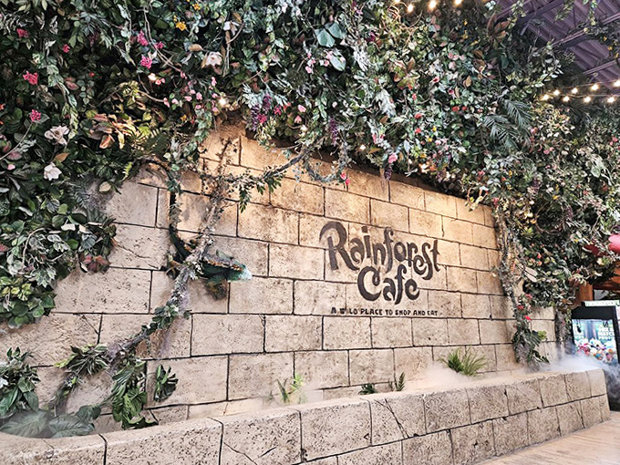 The entrance wall, adorned with cascading plants and the iconic Rainforest Cafe logo, sets the stage for the jungle adventure that awaits inside.