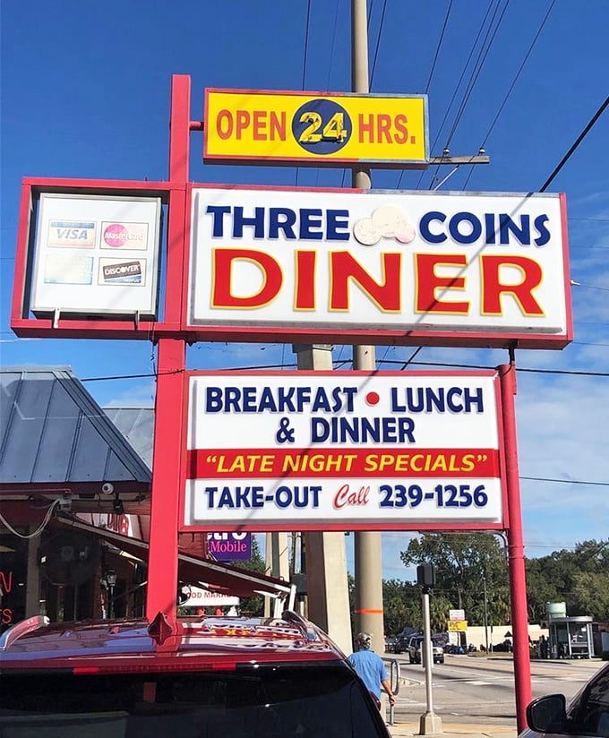 The iconic Three Coins sign glows like a beacon in the night, promising 24-hour access to breakfast nirvana for hungry souls.