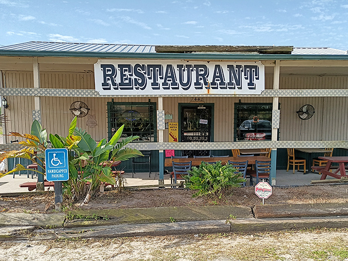 Tropical plants frame the entrance to this roadside haven, where hungry travelers and loyal locals gather. The wheelchair accessibility sign ensures everyone can enjoy this culinary treasure.