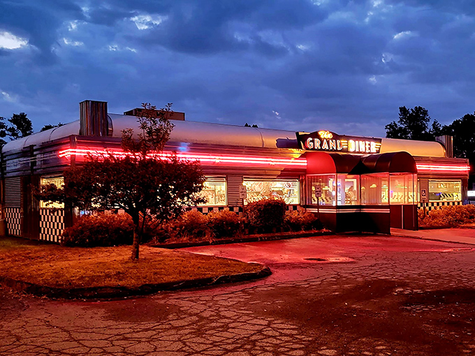 As night falls, The Grand Diner transforms into a glowing beacon of warmth, its neon signs and illuminated windows creating a Edward Hopper-worthy scene.