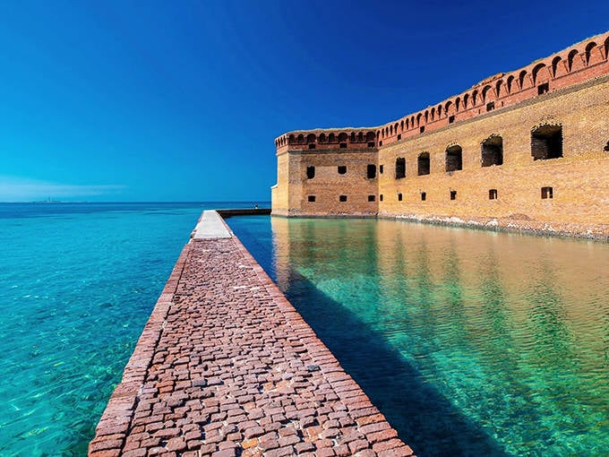 Fort Jefferson's massive brick walls rise from turquoise waters like a mirage, with a stone walkway leading visitors into this island fortress paradise.