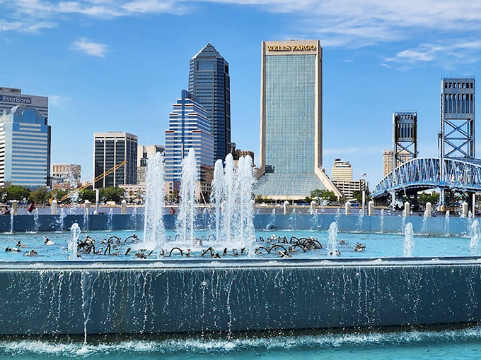 Daytime reveals Friendship Fountain's impressive scale, with powerful jets creating a refreshing mist as downtown Jacksonville towers watch from behind.