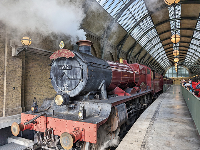Steam billows dramatically around the magnificent red engine as it waits for eager passengers in the vaulted station.