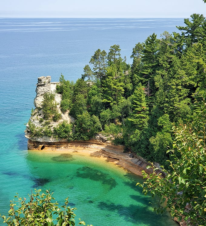 Miners Castle stands sentinel above turquoise waters, its weathered face telling stories of millennia while kayakers explore its majestic base.