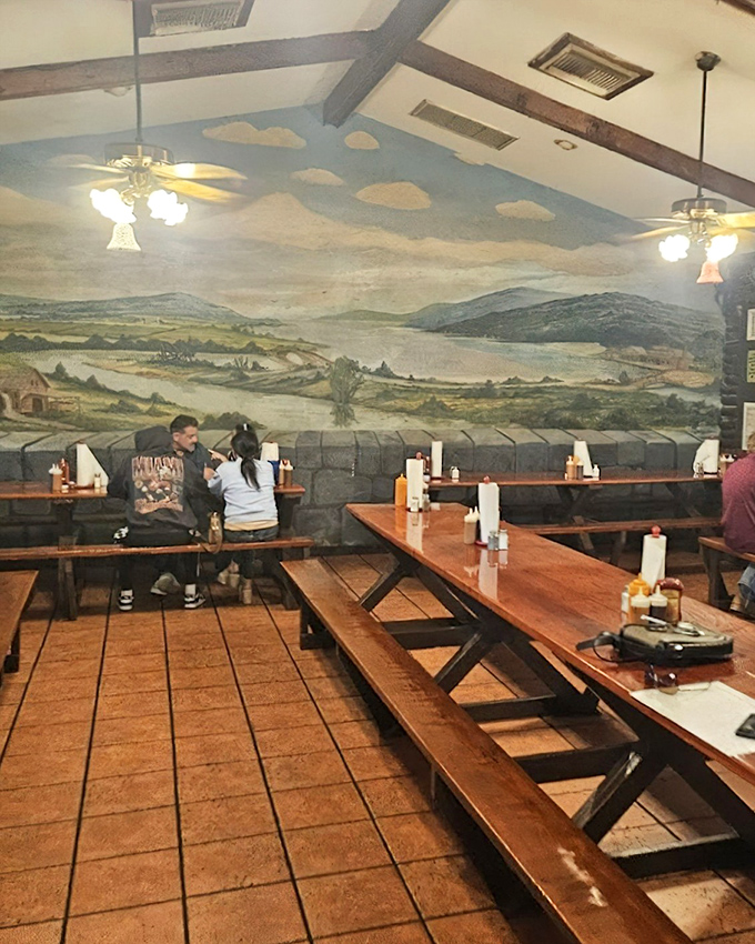 Inside, rustic charm meets barbecue tradition with picnic-style seating beneath a stunning pastoral mural that transports diners to simpler times.