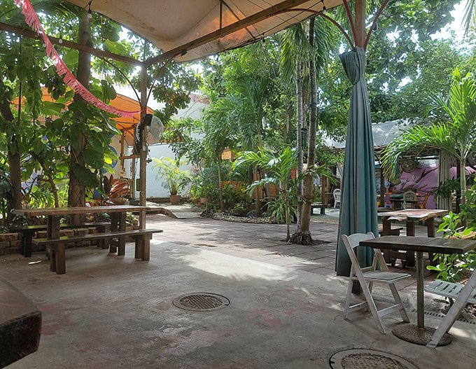 Nature becomes the dining room as wooden benches nestle among tropical plants, creating a backyard Caribbean feast vibe miles from any island.