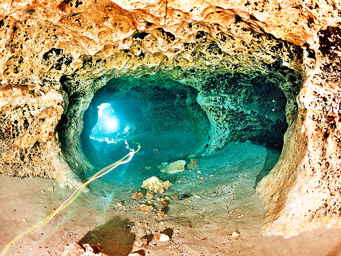 Peering into the underwater cave system reveals a mysterious blue world where sunlight creates dancing patterns on ancient limestone formations.