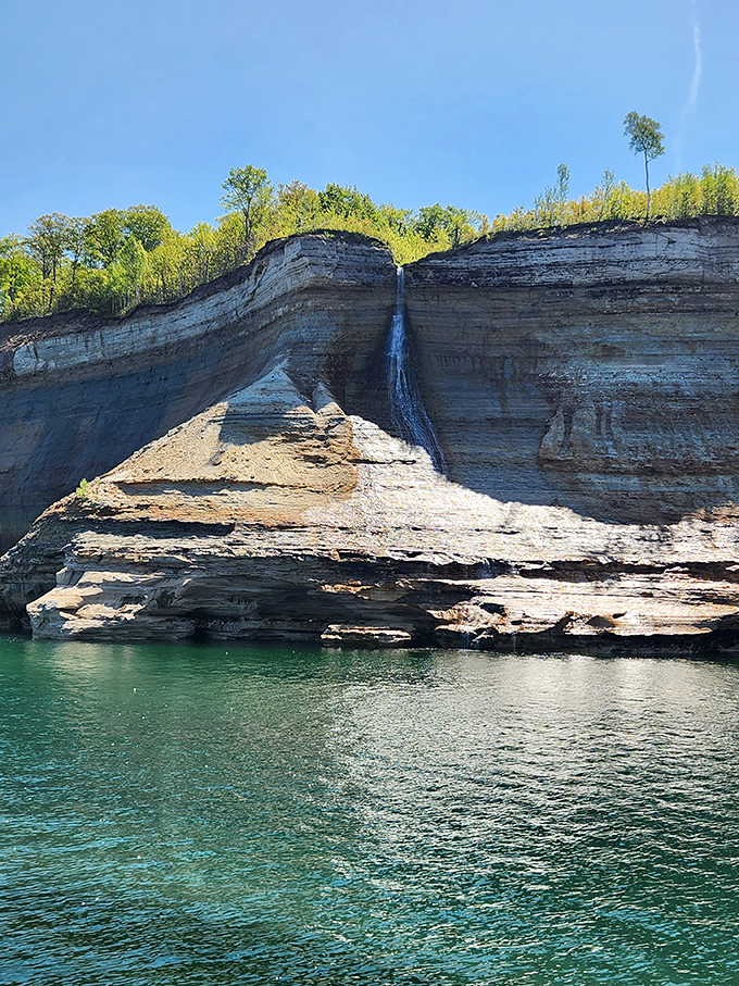A delicate waterfall cascades down ancient rock face, like nature's own version of a beaded curtain against the stone.