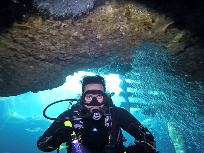 A diver explores the ethereal blue depths, suspended between worlds where sunlight filters through like heavenly spotlights.