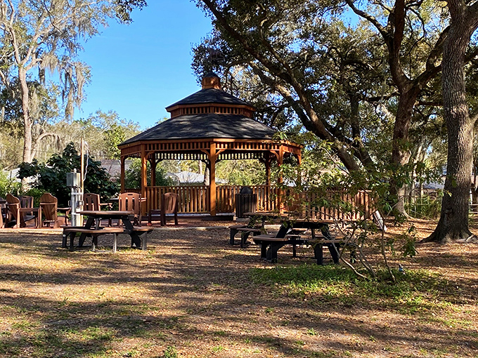 The rustic gazebo stands like a woodland throne room, where picnic tables await forest feasts under dappled sunlight.