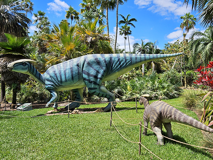 Towering dinosaur sculptures loom among lush palms, blending prehistoric imagination with tropical greenery in a scene where art and nature collide.