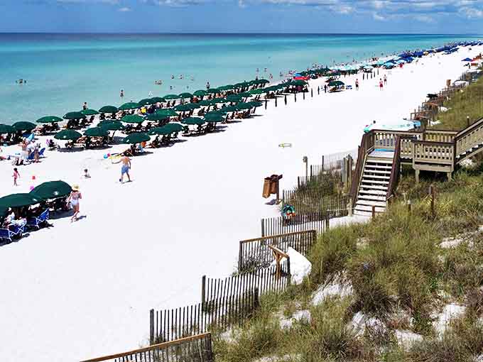 Beach umbrellas dot the shoreline like a rainbow confetti celebration, where sand so white it squeaks underfoot meets the crystal-clear Gulf.
