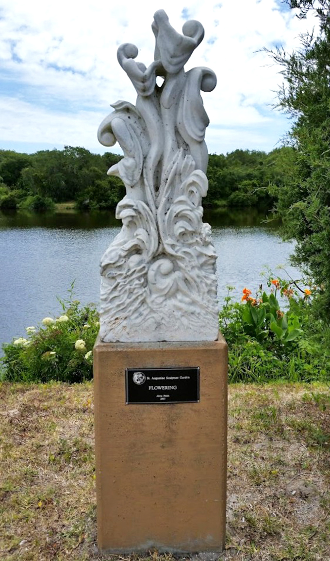 "Flowering" reaches skyward like nature's ghostly ballet dancer &ndash; white stone captures movement in stillness beside the lake's reflective surface.