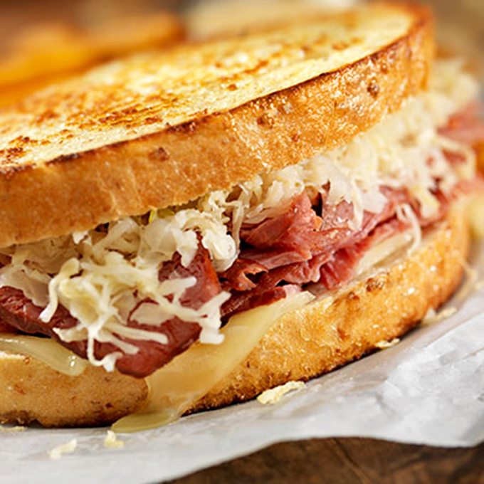 The legendary Reuben in all its glory &ndash; layers of tender corned beef, tangy sauerkraut, and melted Swiss cheese embraced by perfectly grilled rye bread.