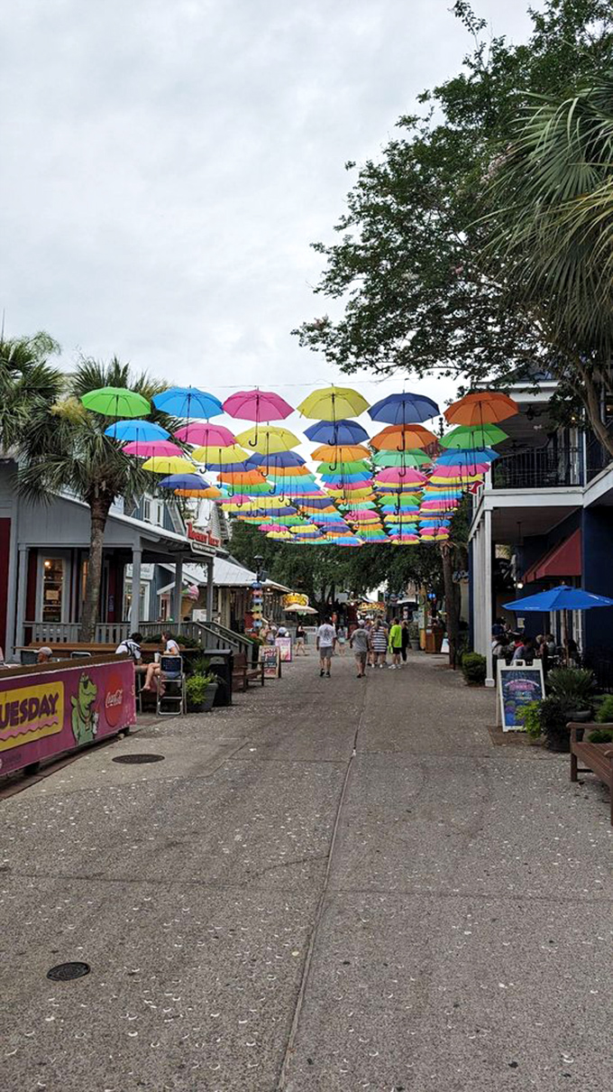 A rainbow canopy of umbrellas hovers above pedestrians, proving that even rain protection can be an art form in this whimsical village.
