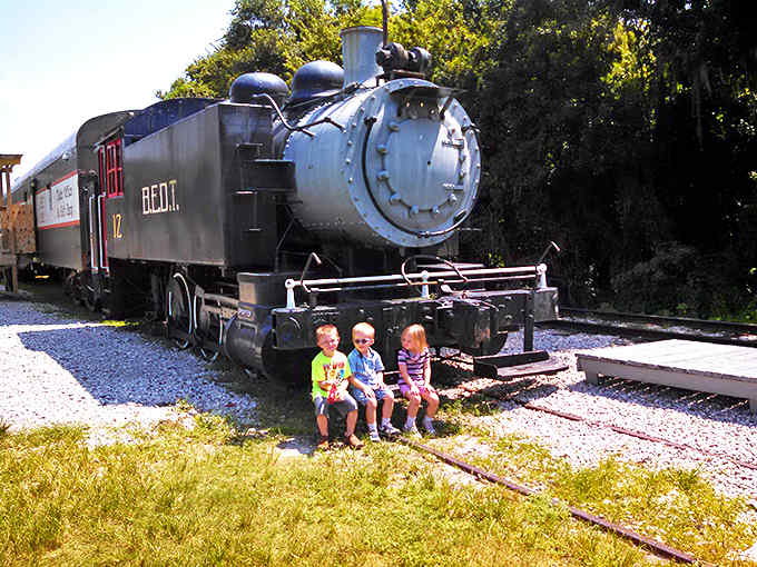 Kids sitting in front of the train: Three young conductors-in-training size up the massive BEDT locomotive, their expressions a perfect blend of awe and possibility.