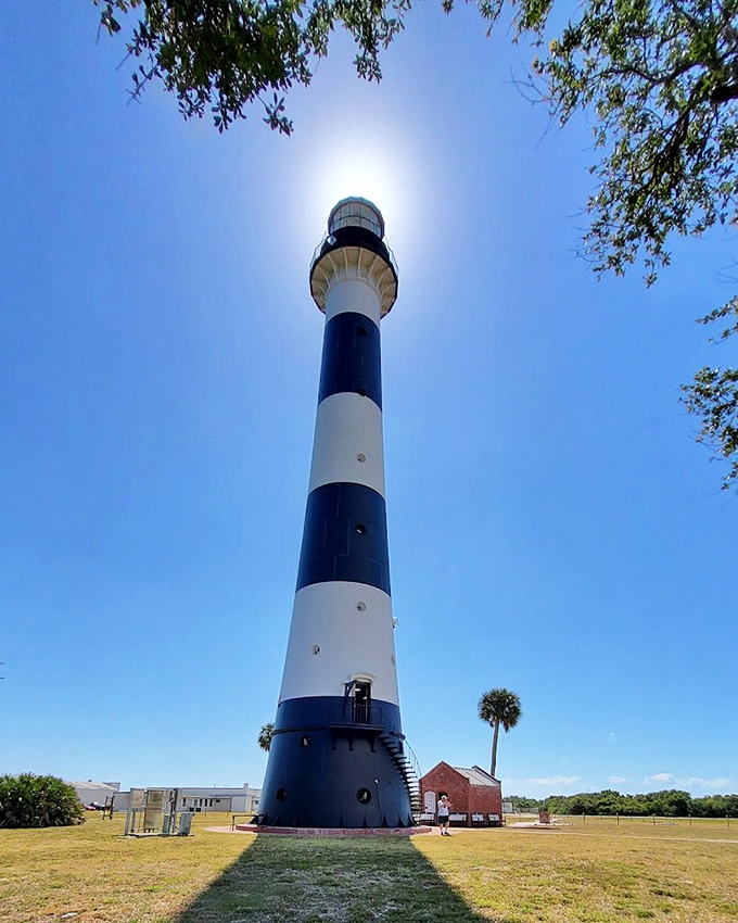 Cape Canaveral Lighthouse stands tall amid tropical greenery, its red top and waterfront location creating a quintessential Florida coastal scene.
