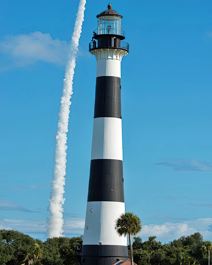 The historic Cape Canaveral Lighthouse watches over a rocky shoreline, its bright red top a beacon for ships navigating Florida's Space Coast.