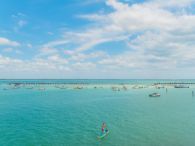 The Boca Grande Sandbar creates a natural swimming pool where boats gather and turquoise waters invite paddleboarders into a postcard-perfect scene.