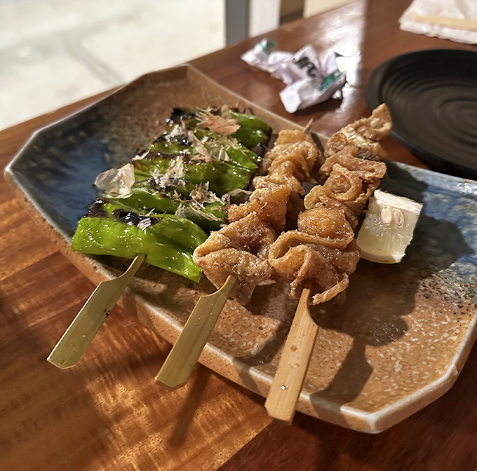 Skewered delights share a plate with vibrant shishito peppers &ndash; a perfect marriage of char, salt, and vegetable sweetness.