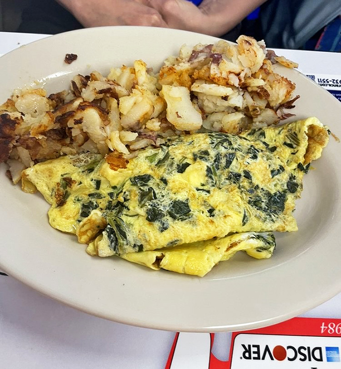 A perfectly folded egg blanket stuffed with vibrant greens and tangy cheese, paired with home fries worth fighting over.