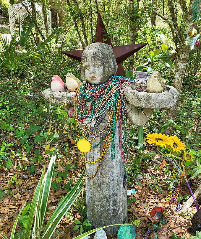 This weathered concrete statue, draped in colorful beads, stands as the camp's unofficial jewelry model &ndash; accessorizing has clearly transcended the physical realm.