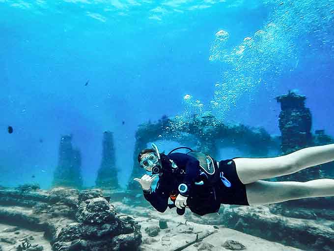 A diver glides through crystal waters, exploring the Neptune Memorial Reef with childlike wonder and respectful curiosity.
