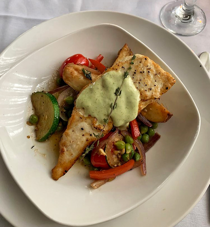 Delicate white fish perches atop a colorful medley of seasonal vegetables, crowned with an herb sauce that adds both brightness and depth.