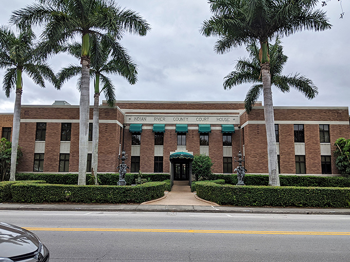 Stately royal palms frame the historic Indian River County Courthouse, its brick fa&ccedil;ade and green awnings embodying old Florida dignity.