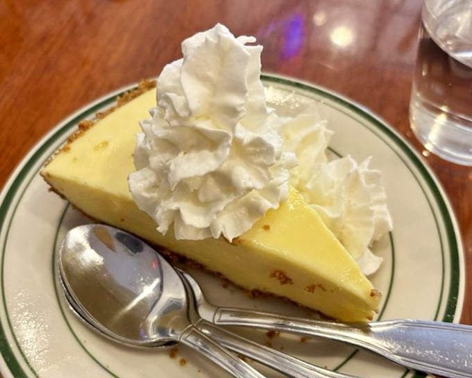 Delicious slice of creamy key lime pie topped with fluffy whipped cream, beautifully presented with two spoons for a perfect shared treat.