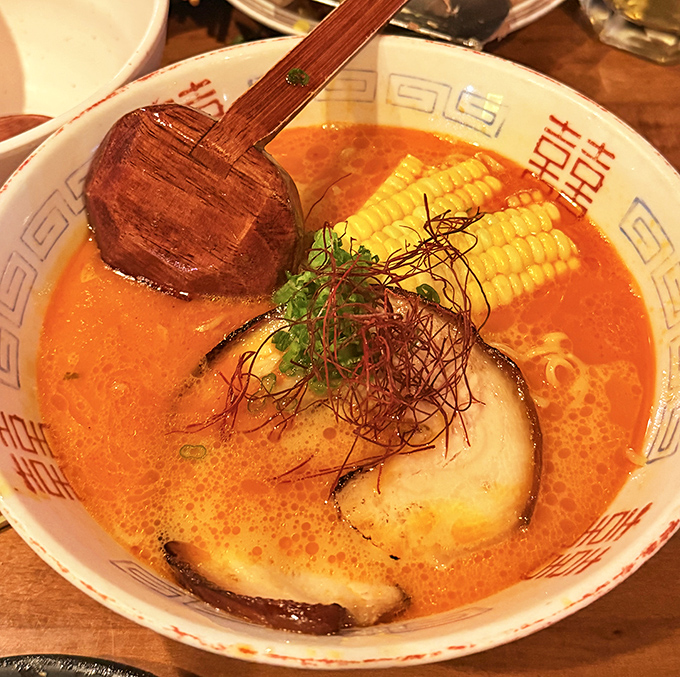 A steaming bowl of ramen shines with rich broth, sweet corn, and tender pork slices.