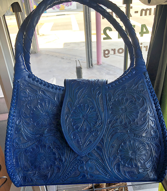 This blue leather shoulder bag with intricate floral tooling whispers of craftsmanship from another era &ndash; the kind of accessory that collects compliments faster than it collected dust.