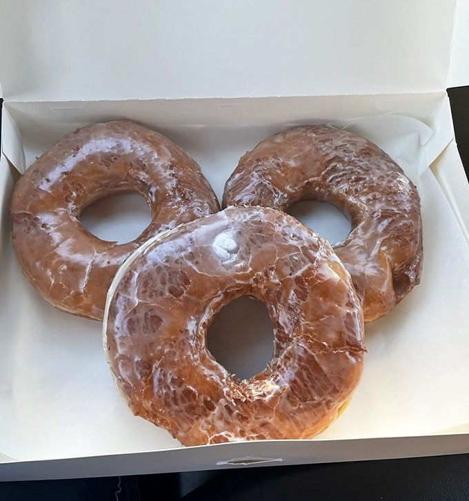 These glazed donuts glisten with that perfect sweet shell that shatters slightly between your teeth before revealing cloud-like interiors.