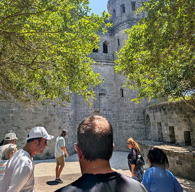 Tourists gaze upward at towering stone walls, their modern attire creating a delightful time-warp against the medieval backdrop.