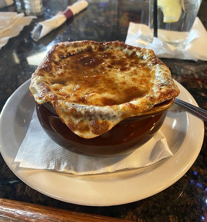 The French onion soup arrives like a bubbling cauldron of comfort, with a golden cheese crown that stretches with each spoonful.