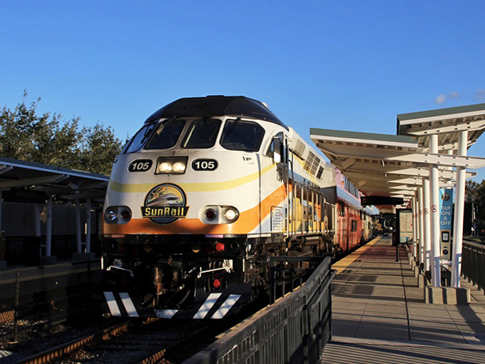 The approaching SunRail locomotive announces itself with a gentle horn, its bright livery bringing a pop of color to this charming station.