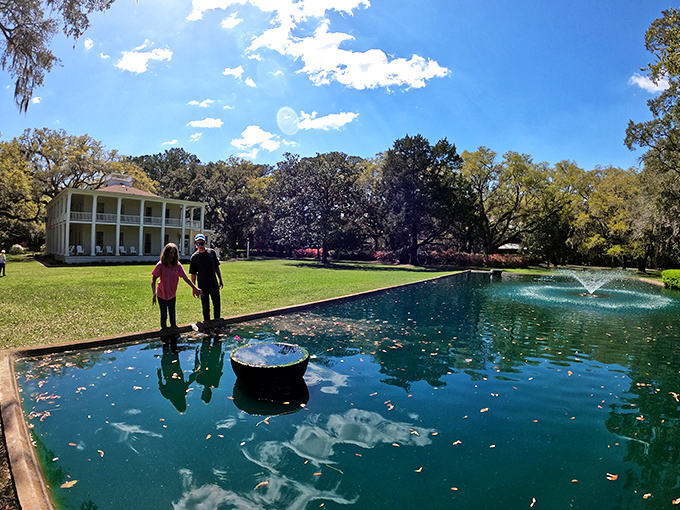 Visitors reflect by the serene pond, where water mirrors sky and mansion in a perfect tableau of natural and human-made beauty.