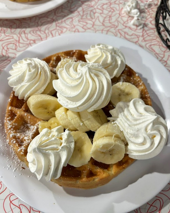Golden waffles cradle fresh banana slices and pillowy whipped cream peaks &ndash; breakfast that blurs the line into dessert territory without apology.