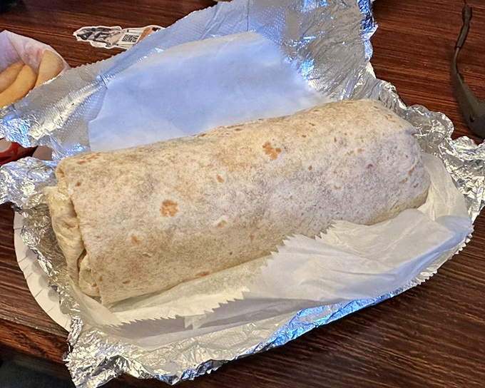 The flour tortilla MVP, performing heroic feats of structural engineering to contain this massive, foil-wrapped flavor bomb that could feed a small family.