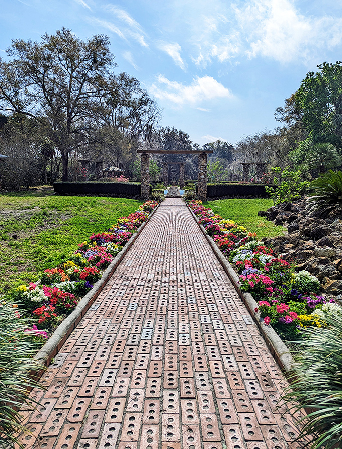 A brick pathway lined with vibrant seasonal blooms leads visitors through formal gardens that contrast beautifully with the wild ravines beyond.